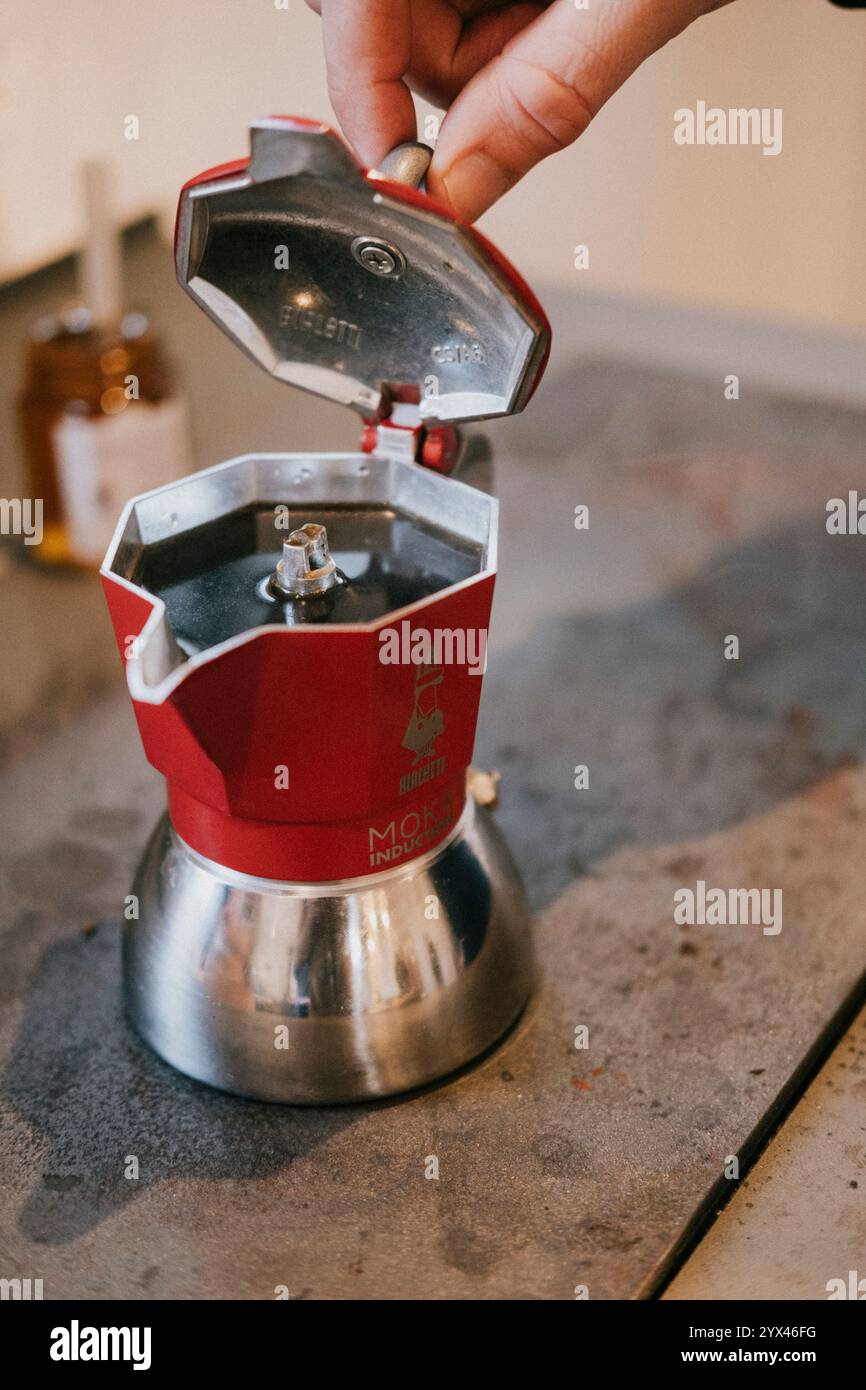 A person is pouring coffee into a red coffee pot. The coffee pot is ...