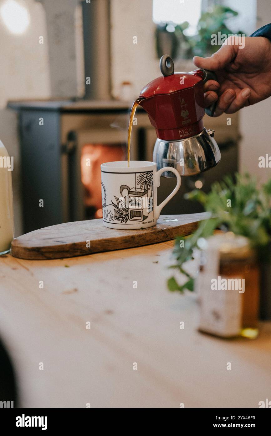 A person is pouring coffee into a mug from a red coffee pot. The coffee ...