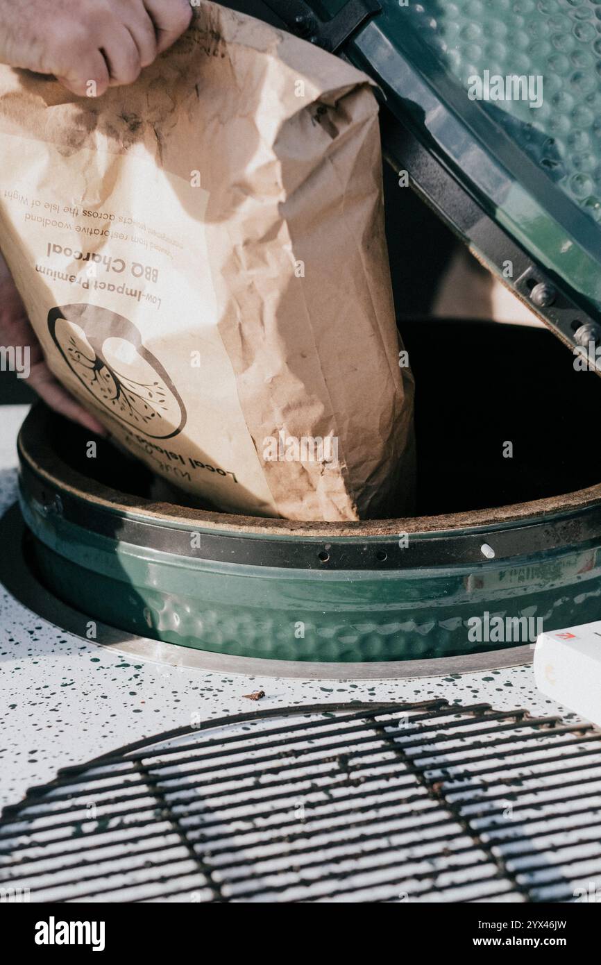 A person is pouring a bag of charcoal into a grill. The bag is brown ...