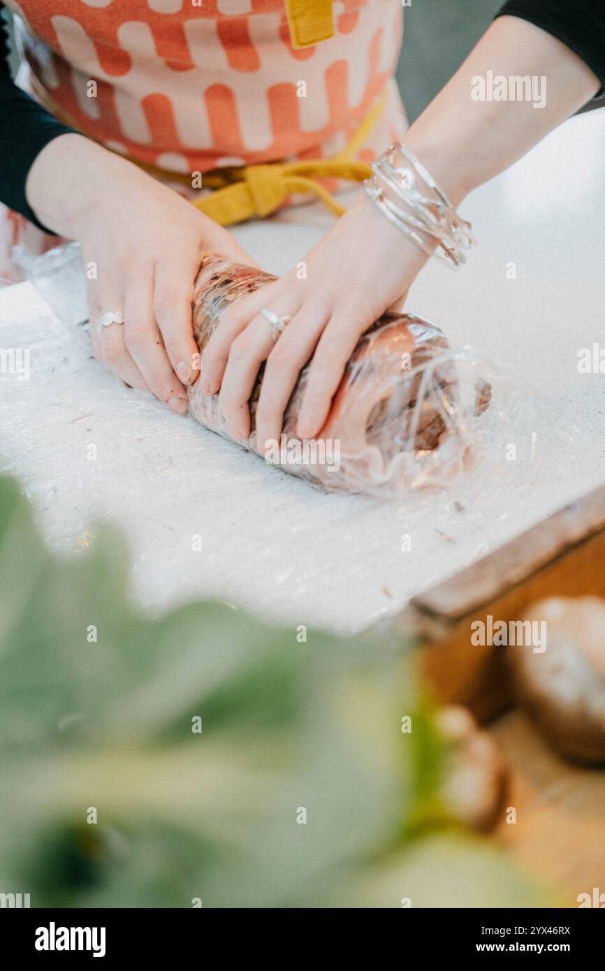 A woman is wrapping food in plastic wrap. The food is a roll of meat ...