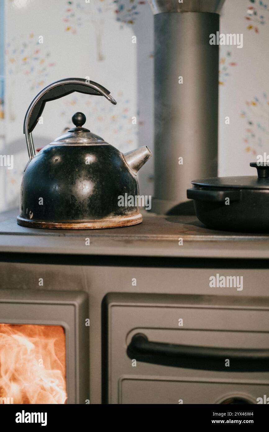 A black tea kettle sits on a stove top. The stove is lit and the fire ...