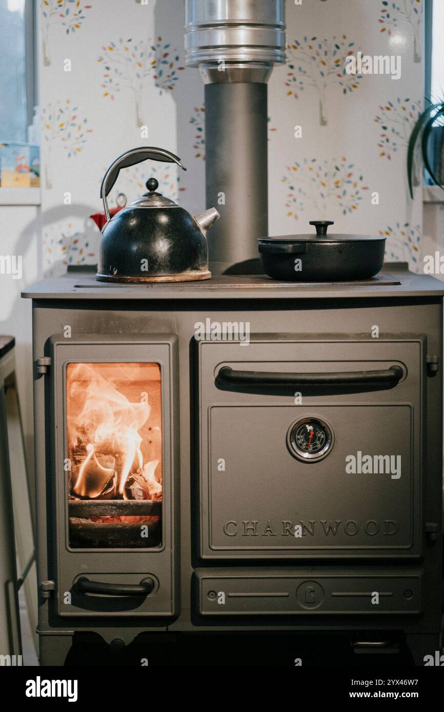A black tea kettle sits on top of a stove with a chimney. The stove is ...