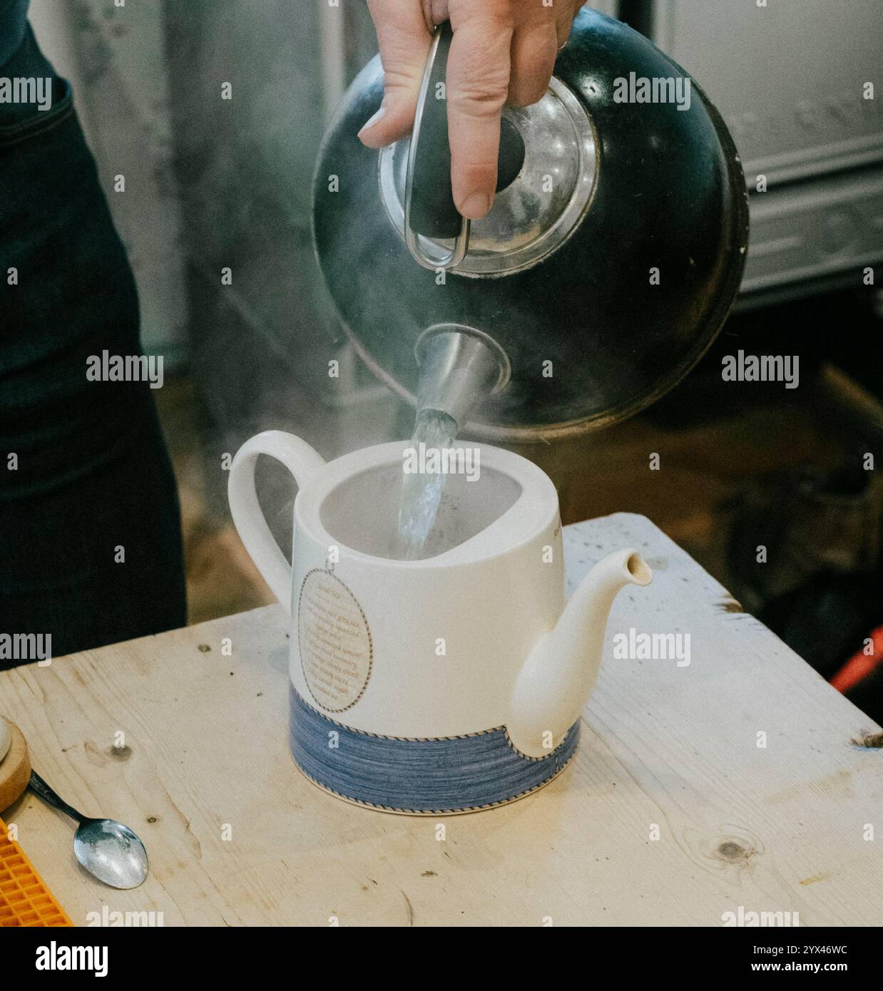 A person is pouring water into a teapot. The teapot is white and blue ...