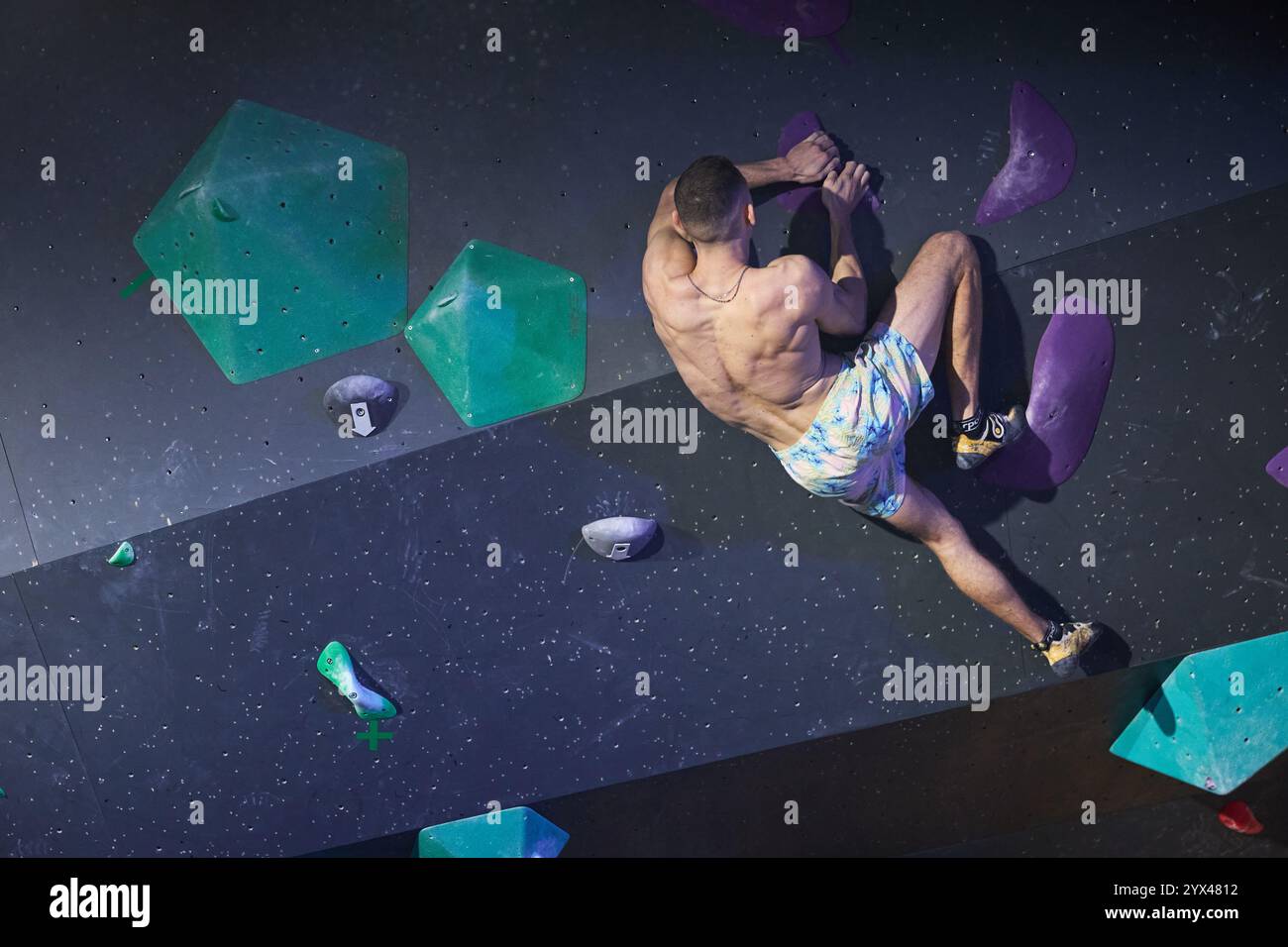 Muscular young man climbing a wall at indoor bouldering competition ...