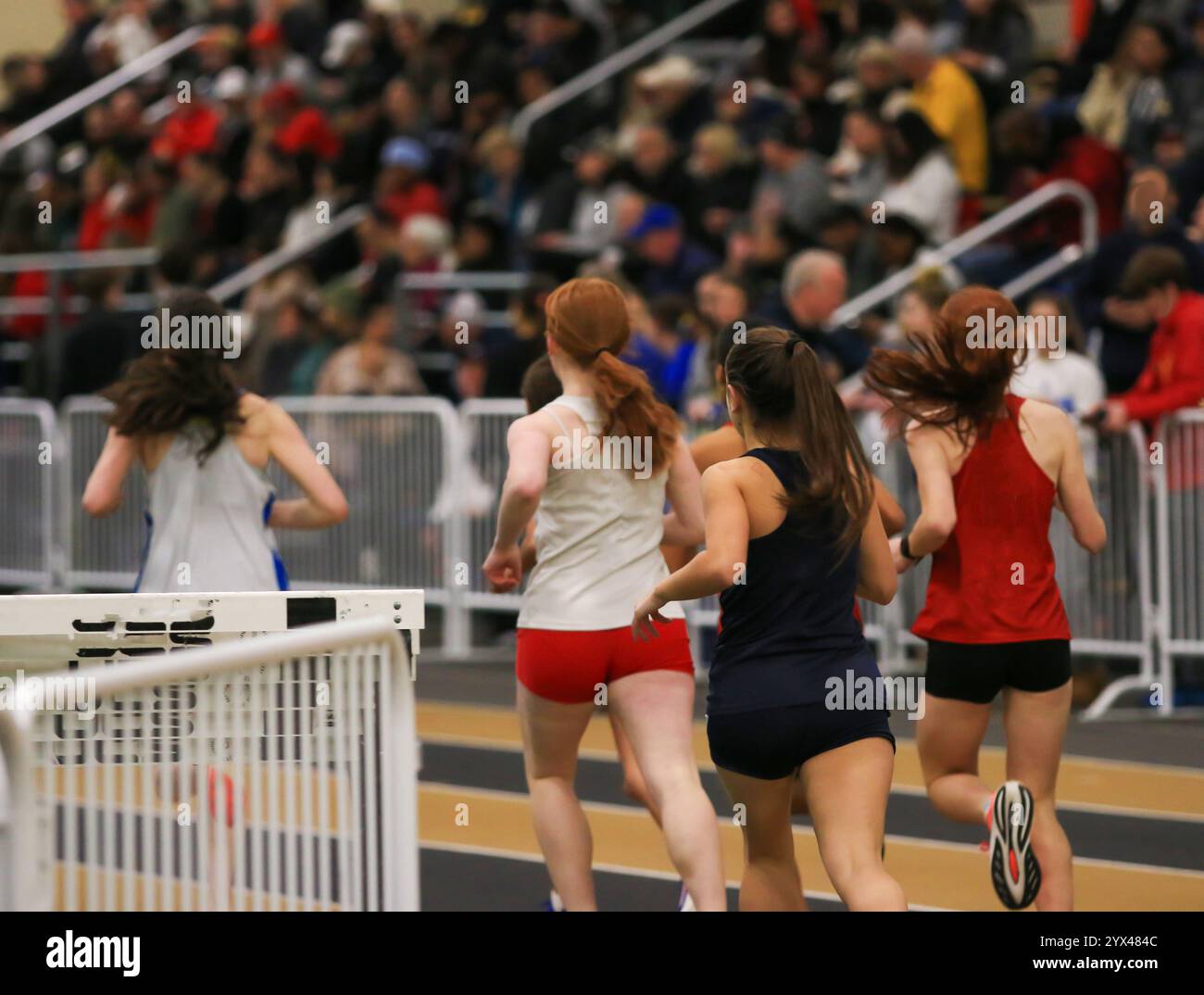 Rear view of several female athletes race on the track, showing ...