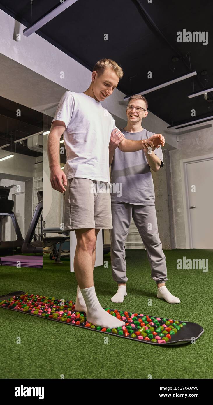 Man walking barefoot on colorful reflexology massage board, assisted by ...
