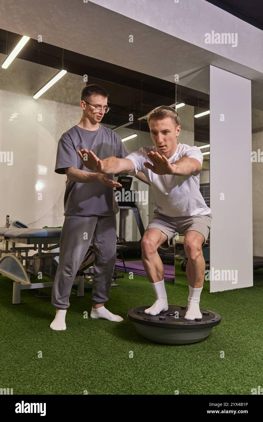 Man performing squats on balance trainer, receiving support and ...