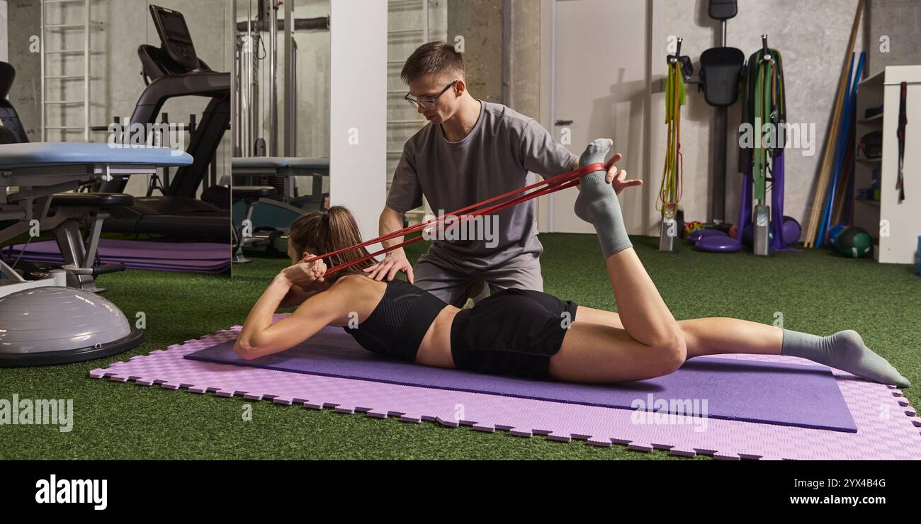 Woman lying on mat, stretching with red resistance band, guided by ...