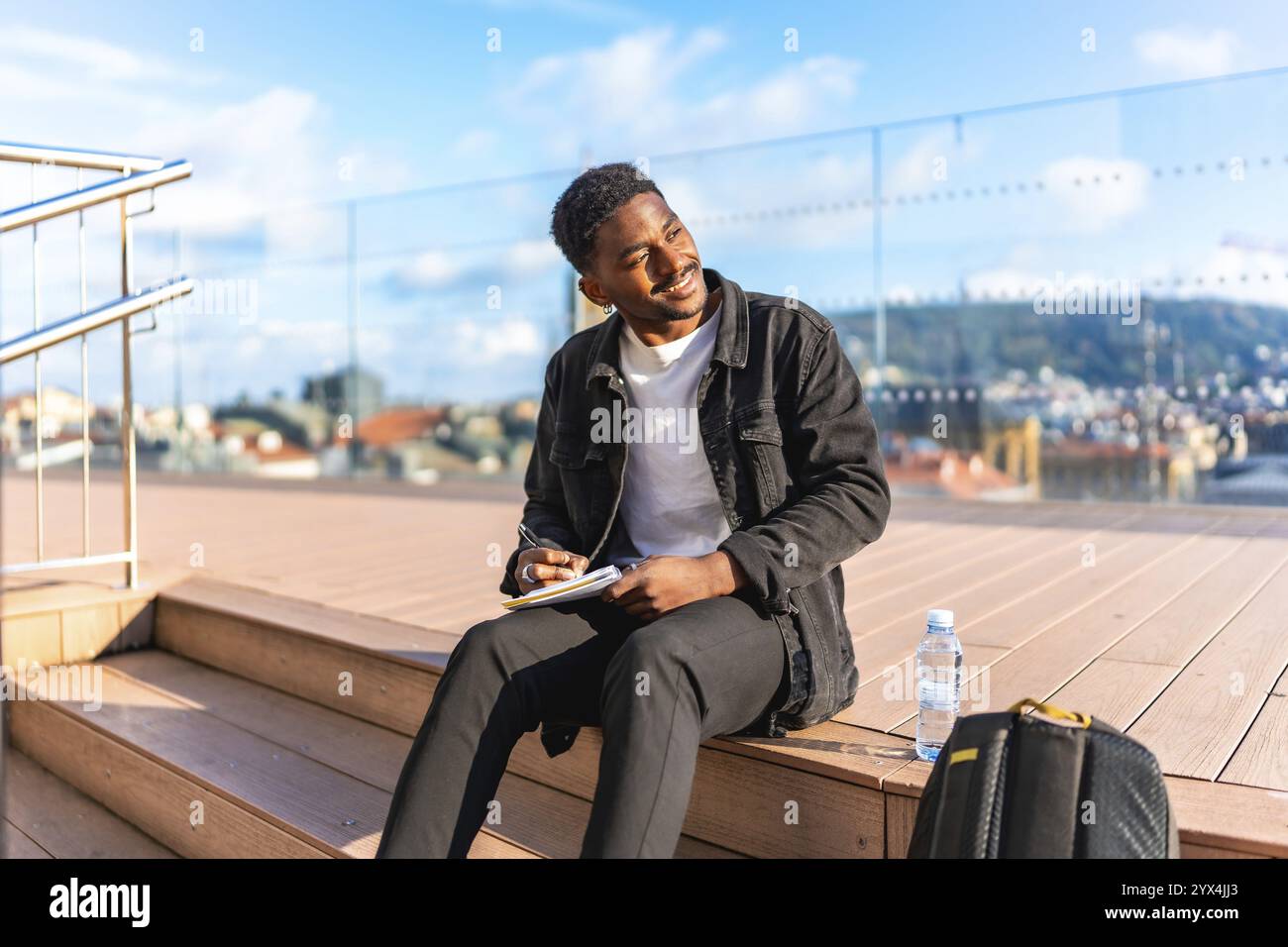 African man writing poems by hand in a notebook sitting on a city ...