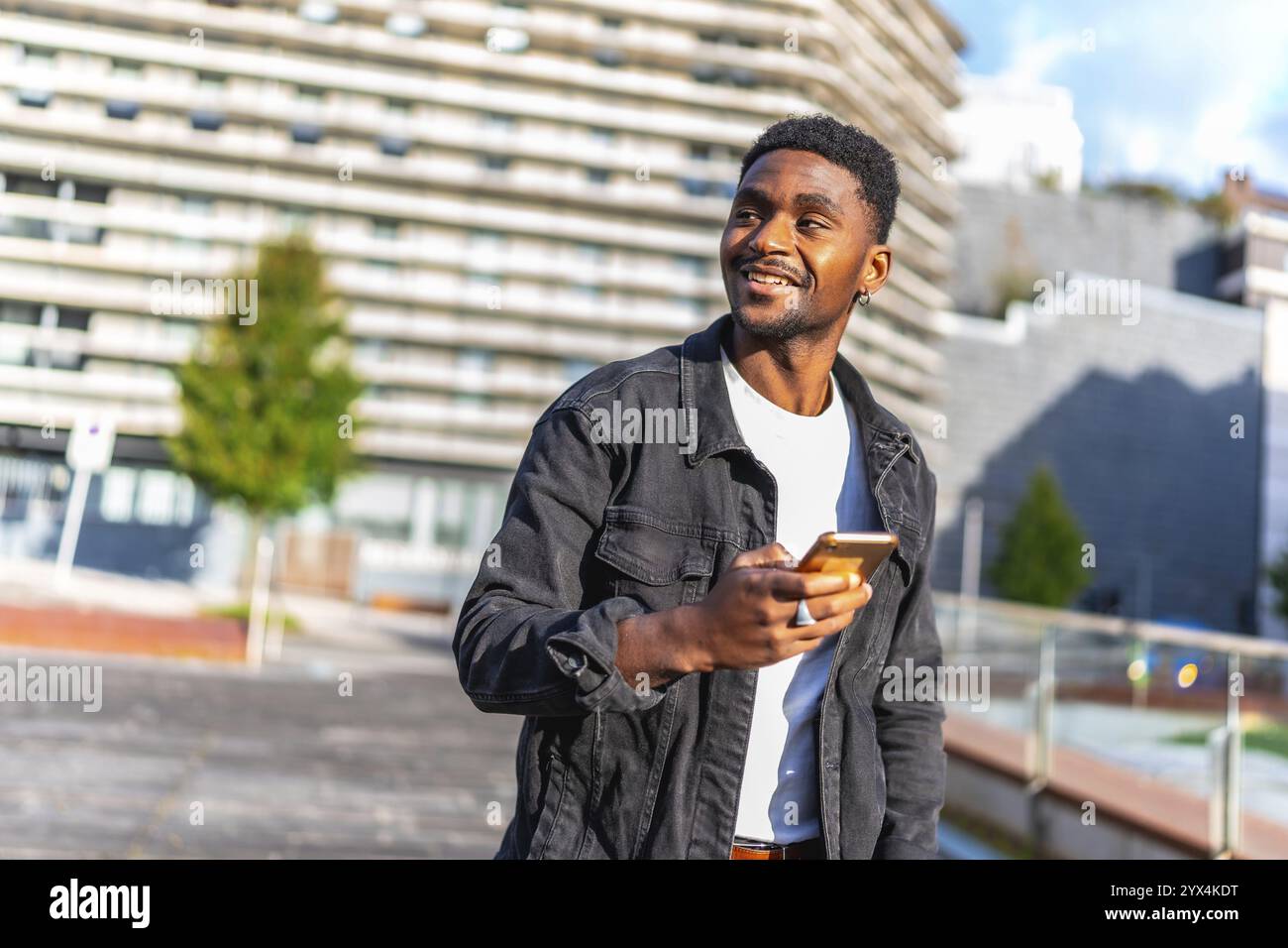 Distracted handsome young african man using mobile app walking along ...