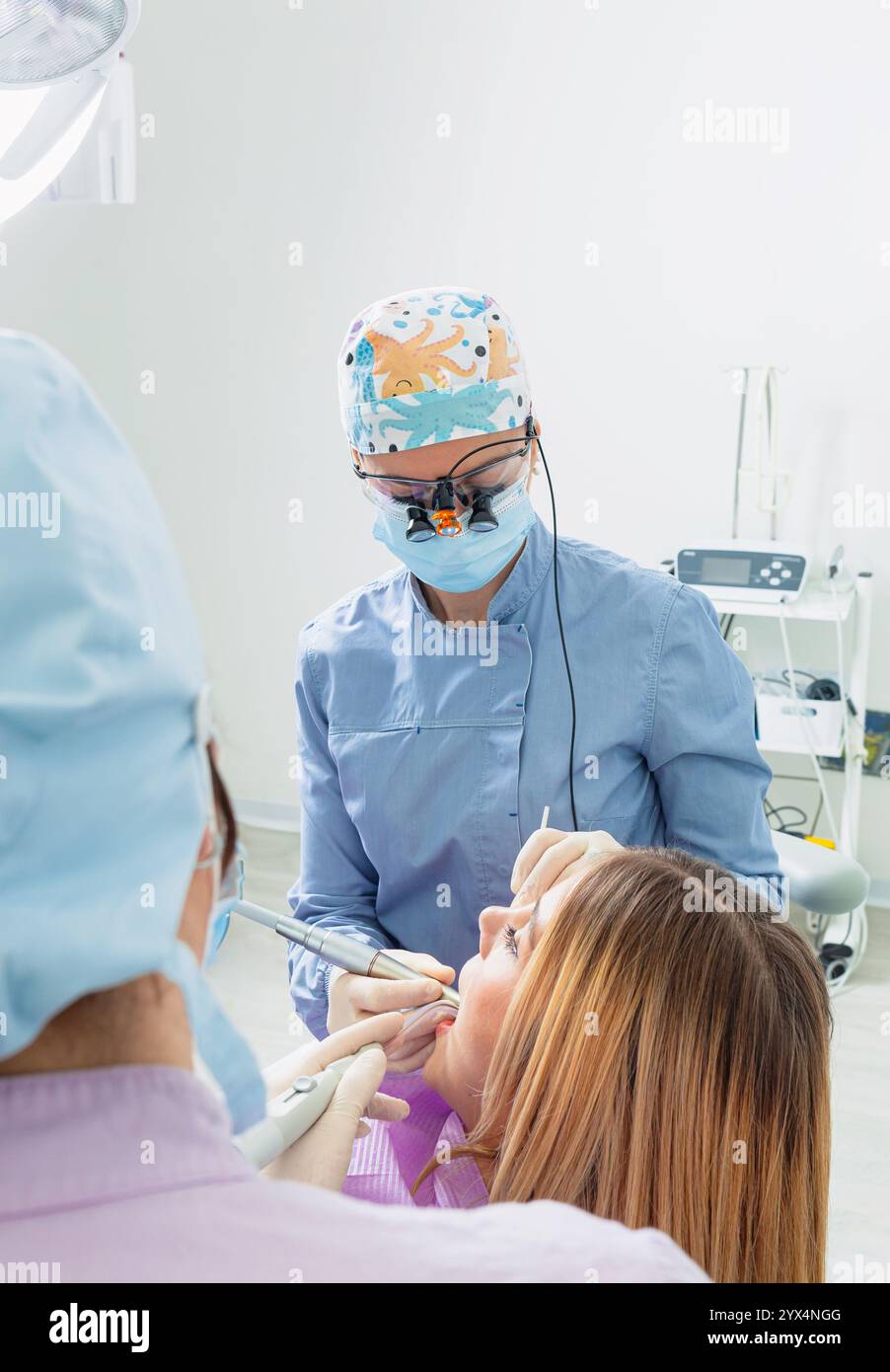 Dentist wearing magnifying glasses operating on patient's teeth with ...