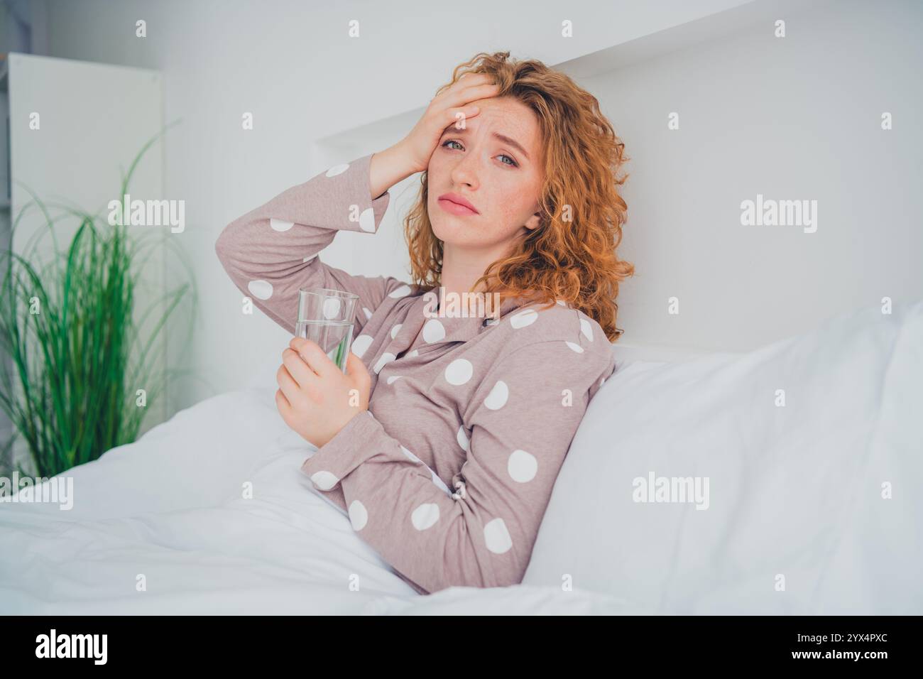 Charming young woman with red hair waking up in bed indoors, holding ...