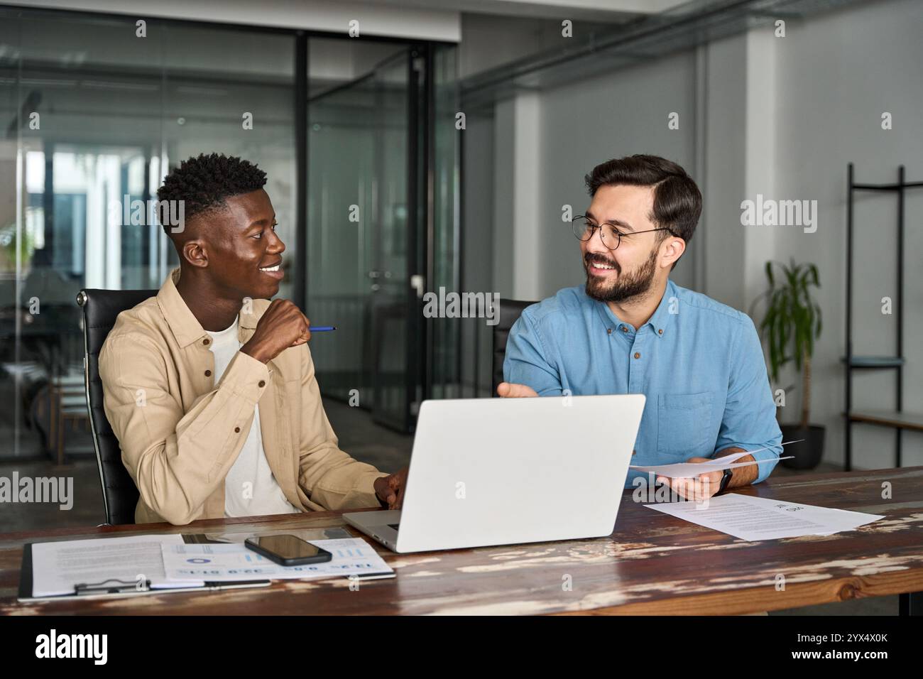 Two busy happy diverse men working on laptops discussing project at ...