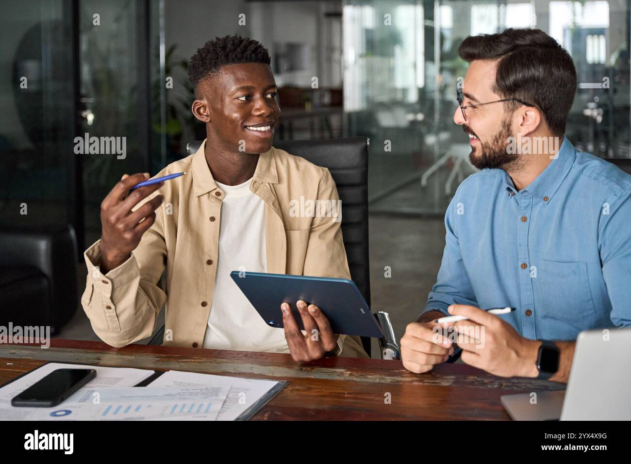 Two happy busy diverse coworkers using tablet working talking in office ...