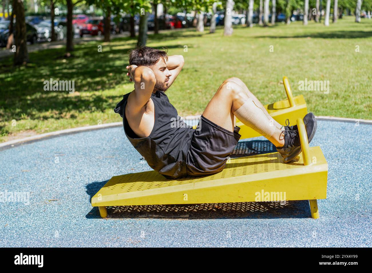Side view of a young man doing sit-ups on outdoor fitness equipment ...