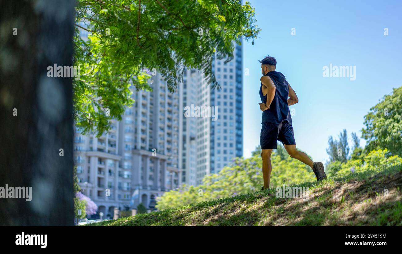 Young athletic man running on hilly trails in a modern city park surrounded by skyscrapers Stock ...