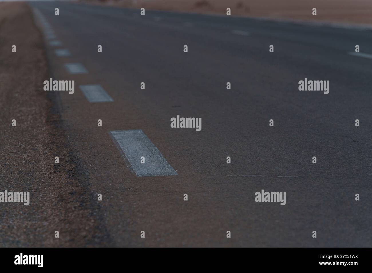 an asphalt road leading through a flat section of desert to the horizon ...