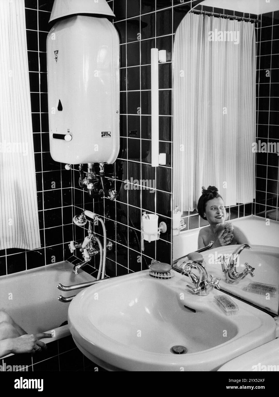 Sitting in a 1950s modern bathtub, a young woman advertises gas-heated ...