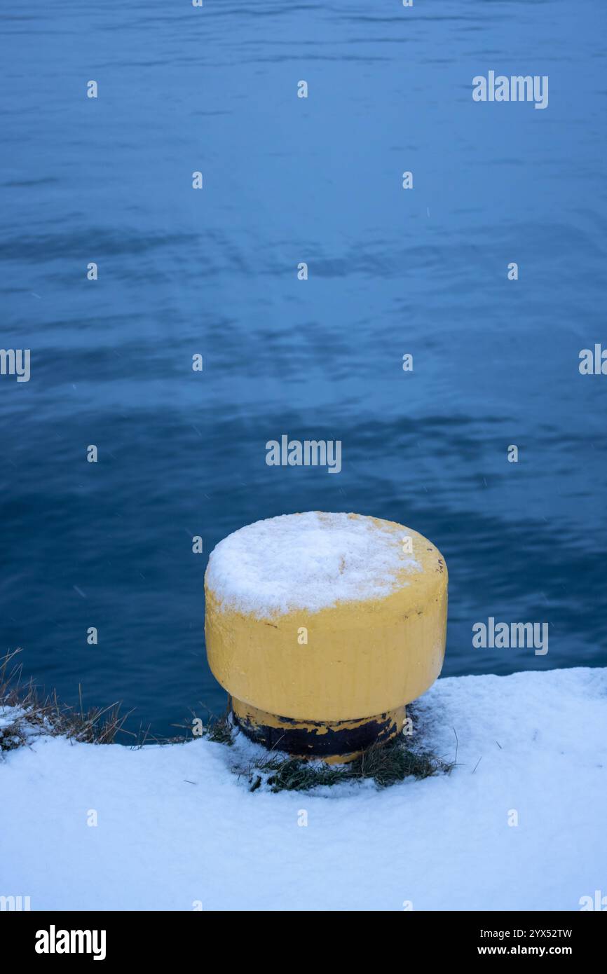 Fresh snow during a snowfall day. Yellow mooring bollard for boats on ...