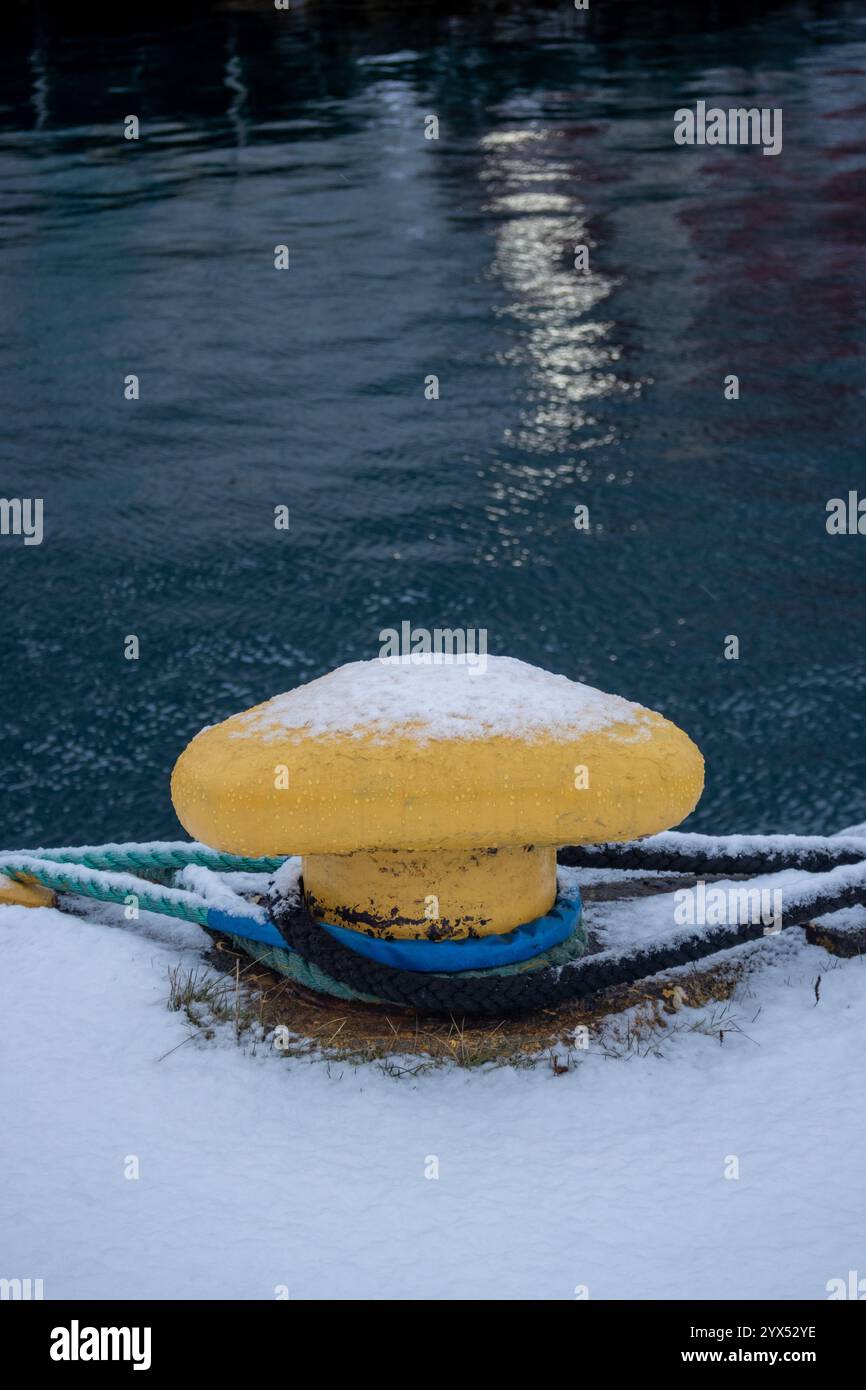 Fresh snow during a snowfall day. Yellow mooring bollard for boats on ...