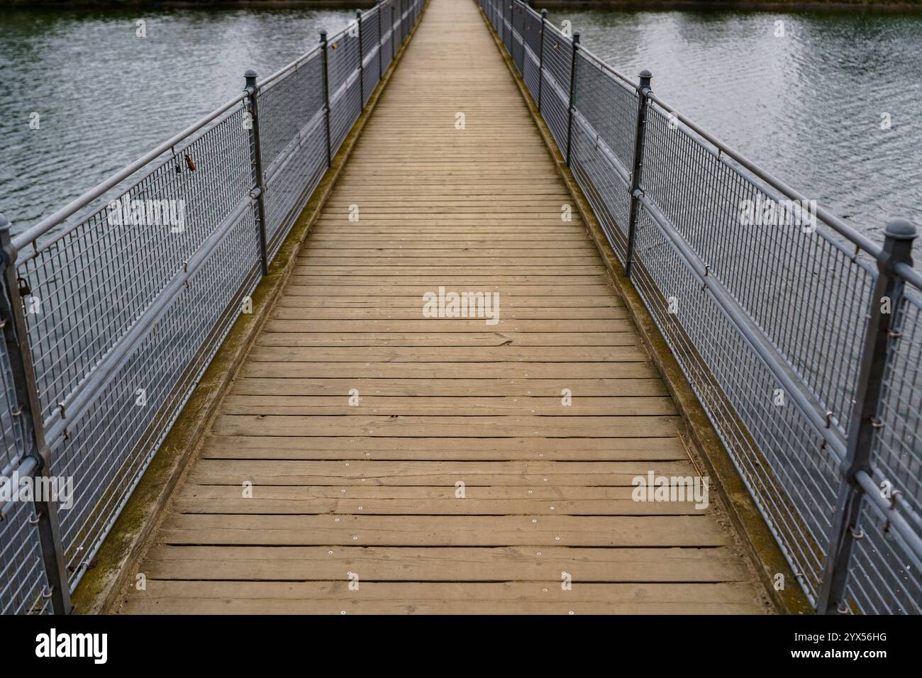 A small wooden and steel pedestrian bridge over a calm body of water ...