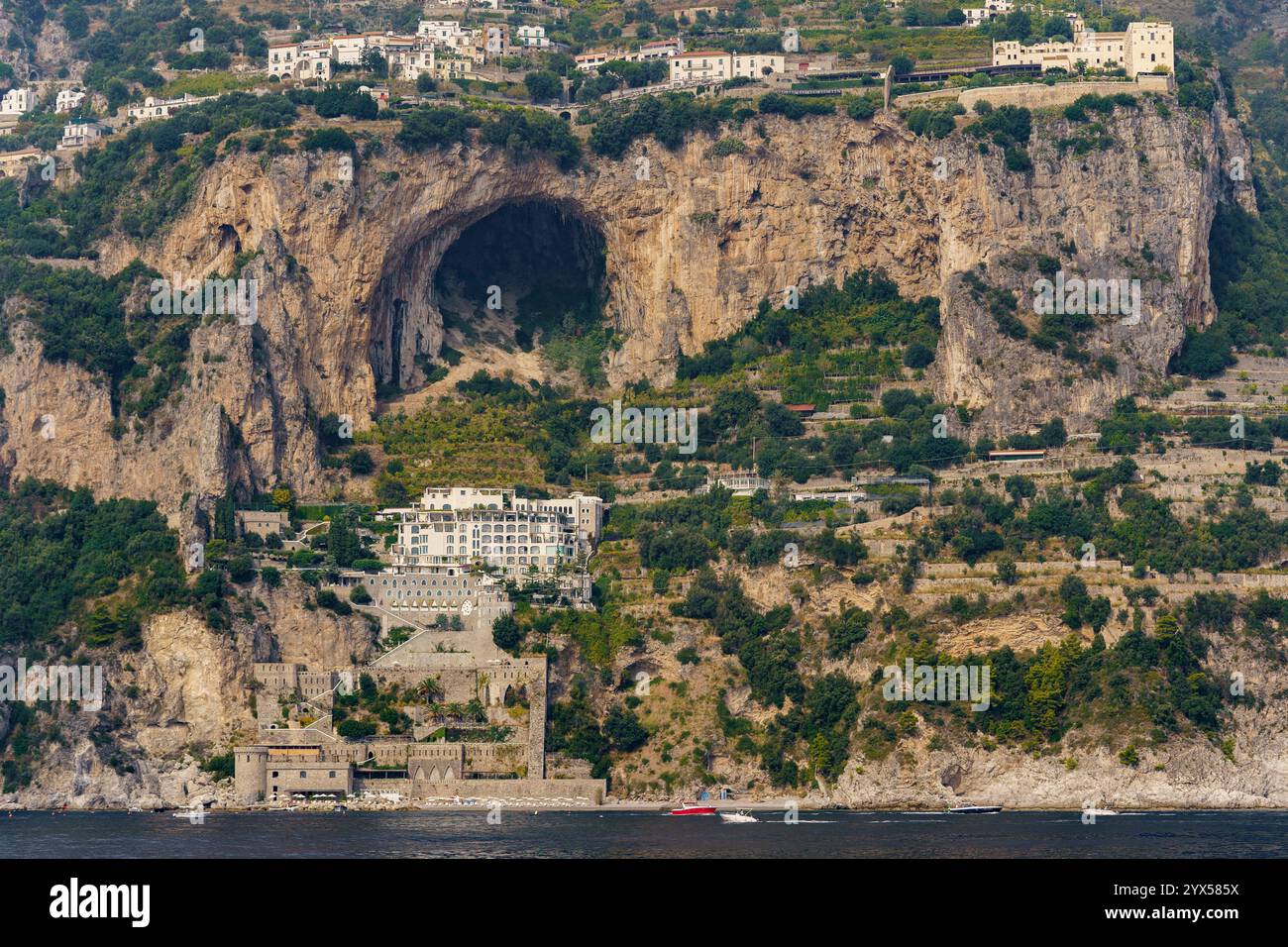 A huge rock cave with an arched ceiling, surrounded by plants and ...