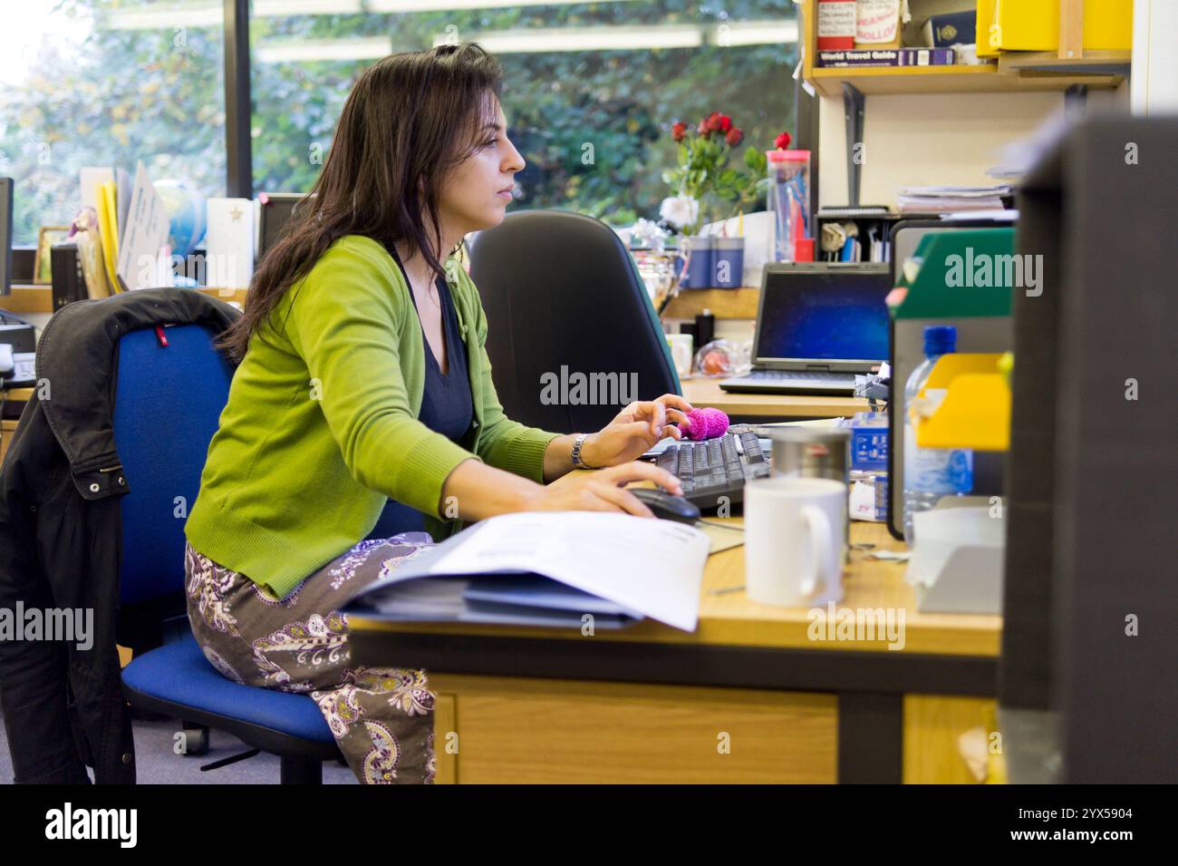 Female teacher working at her desk in staffroom open plan office space ...