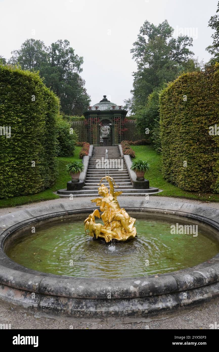 Water fountain with golden sculpture in parterre bordered by deciduous ...