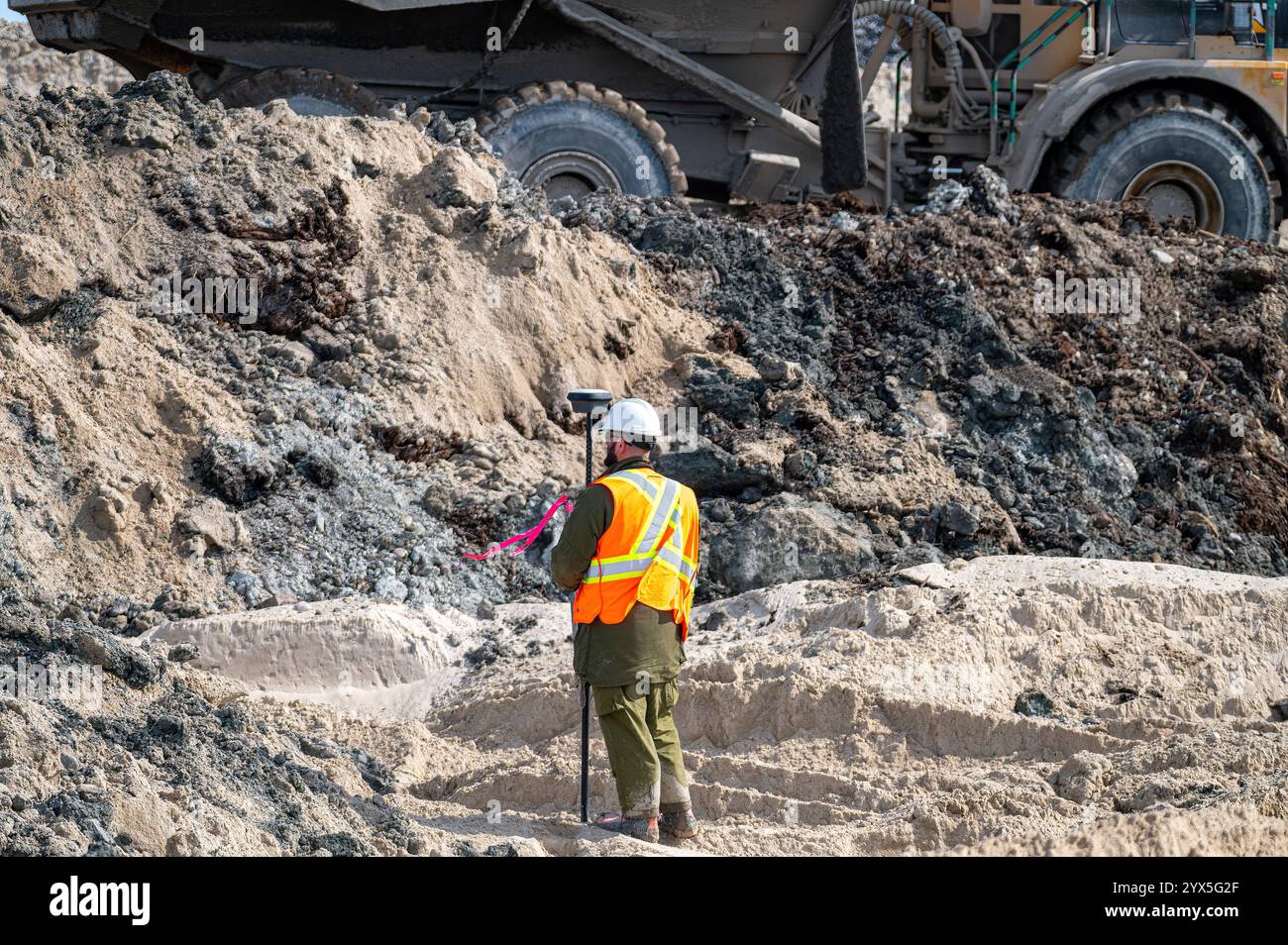 Surveyor carrying out a GPS survey on a construction site, with a dump ...
