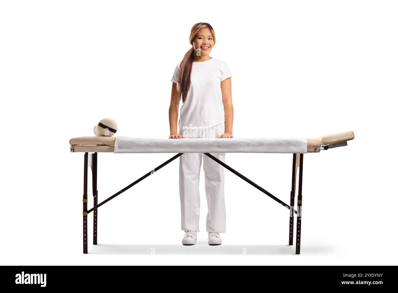 Asian therapist standing behind a massage table isolated on white ...