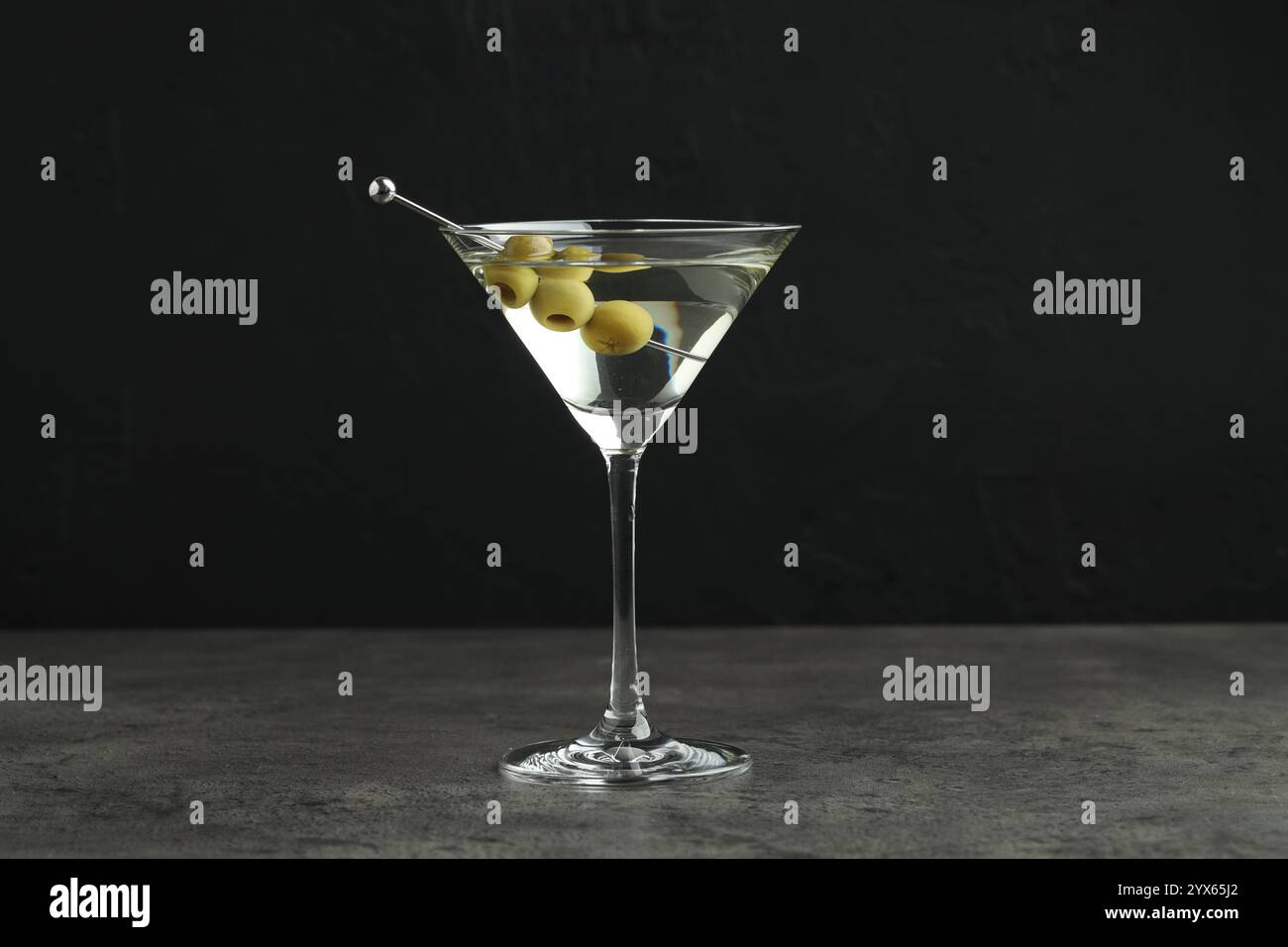 Martini cocktail with olives in glass on grey table against black ...
