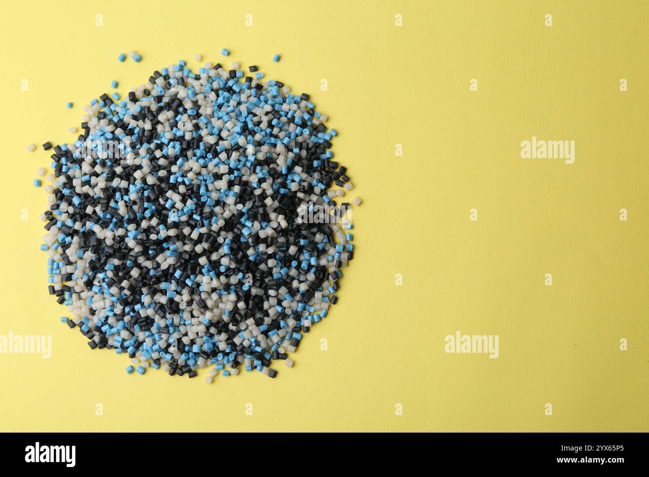 Pile of colorful plastic granules on yellow background, top view. Space ...