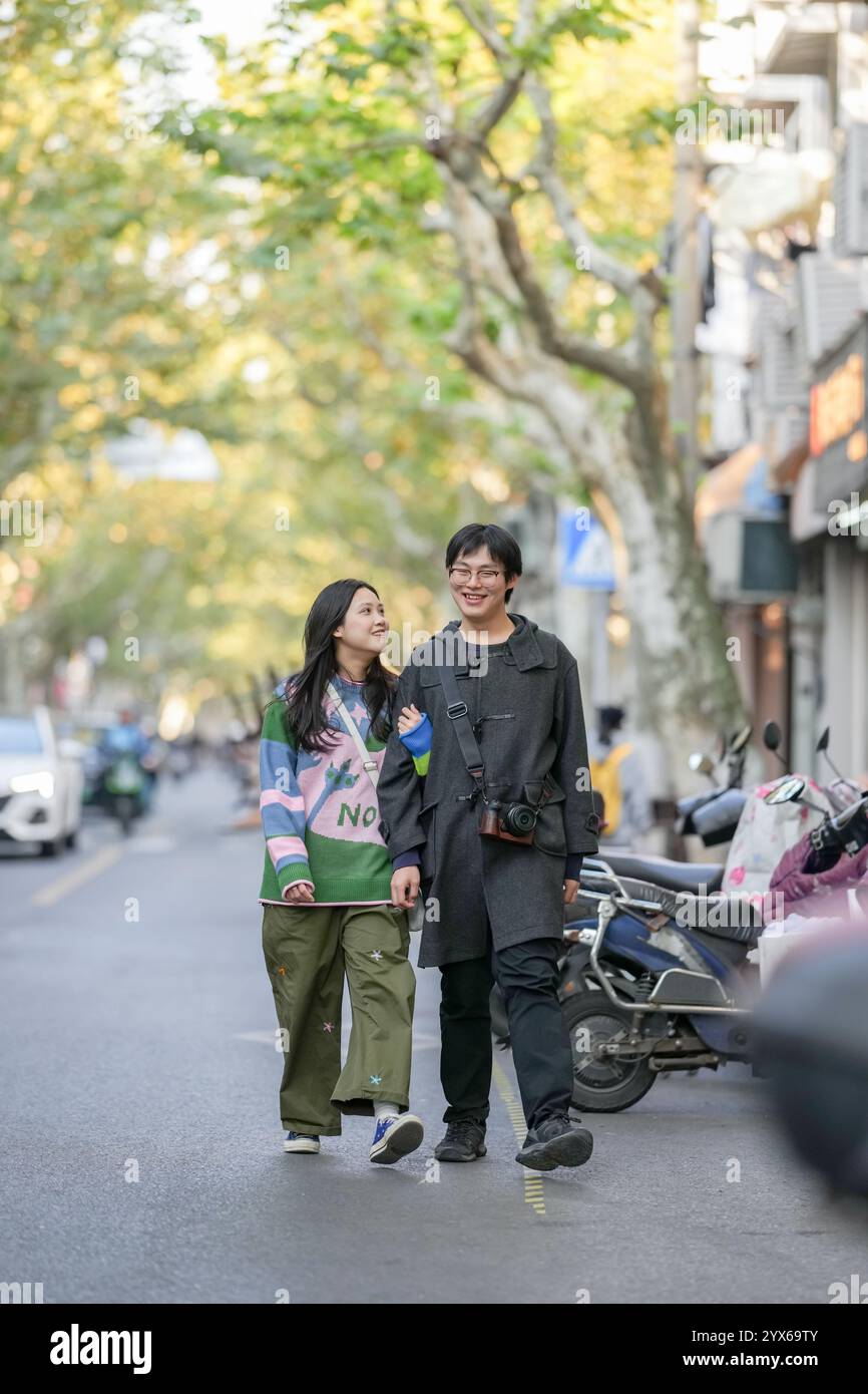 A young Chinese couple in their 20s walks on the sidewalk in Hongkou ...