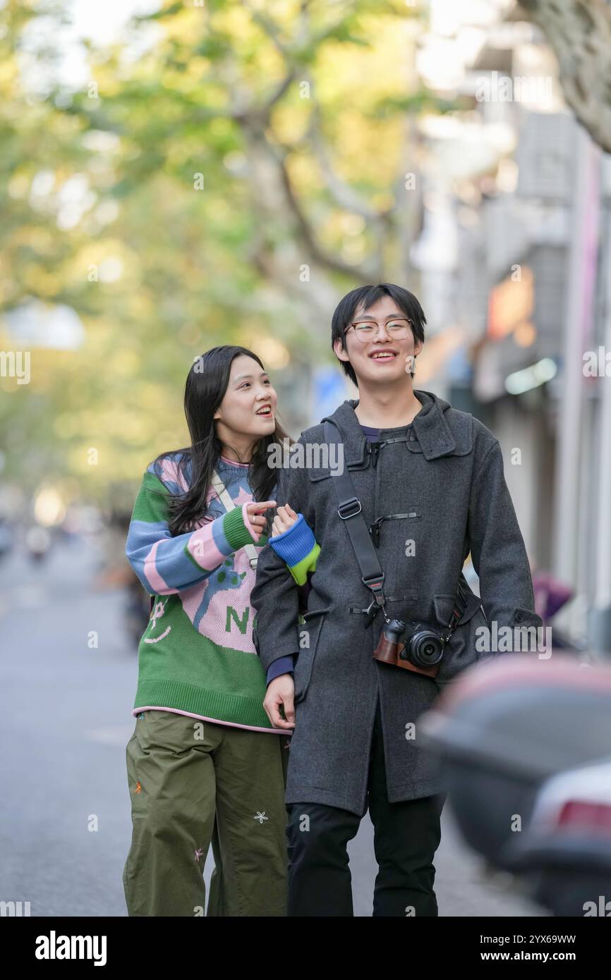 A young Chinese couple in their 20s walks on the sidewalk in Hongkou ...