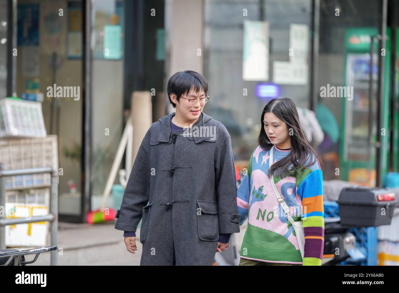 A young Chinese couple in their 20s walks on the sidewalk in Hongkou ...
