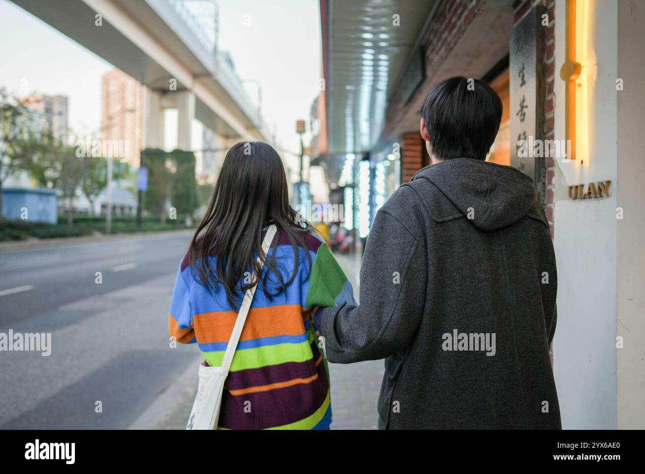 A young Chinese couple in their 20s walking on the sidewalk in Hongkou ...