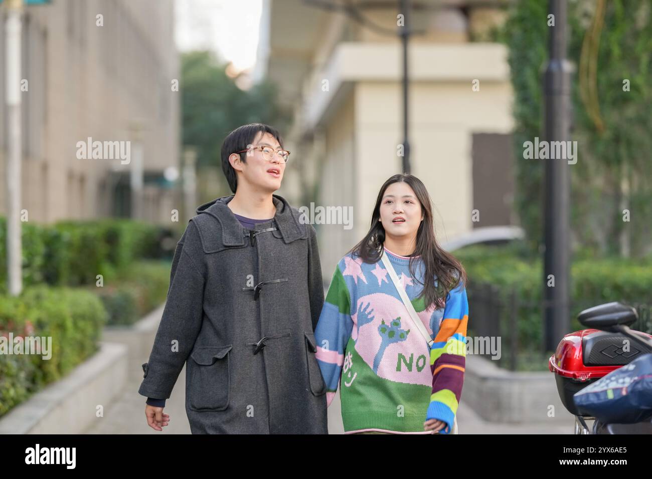A young Chinese couple in their 20s walking on the sidewalk in Hongkou ...