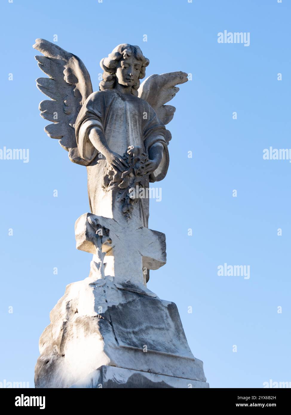 Weathered and stained angel statue standing above a cross. The statue ...