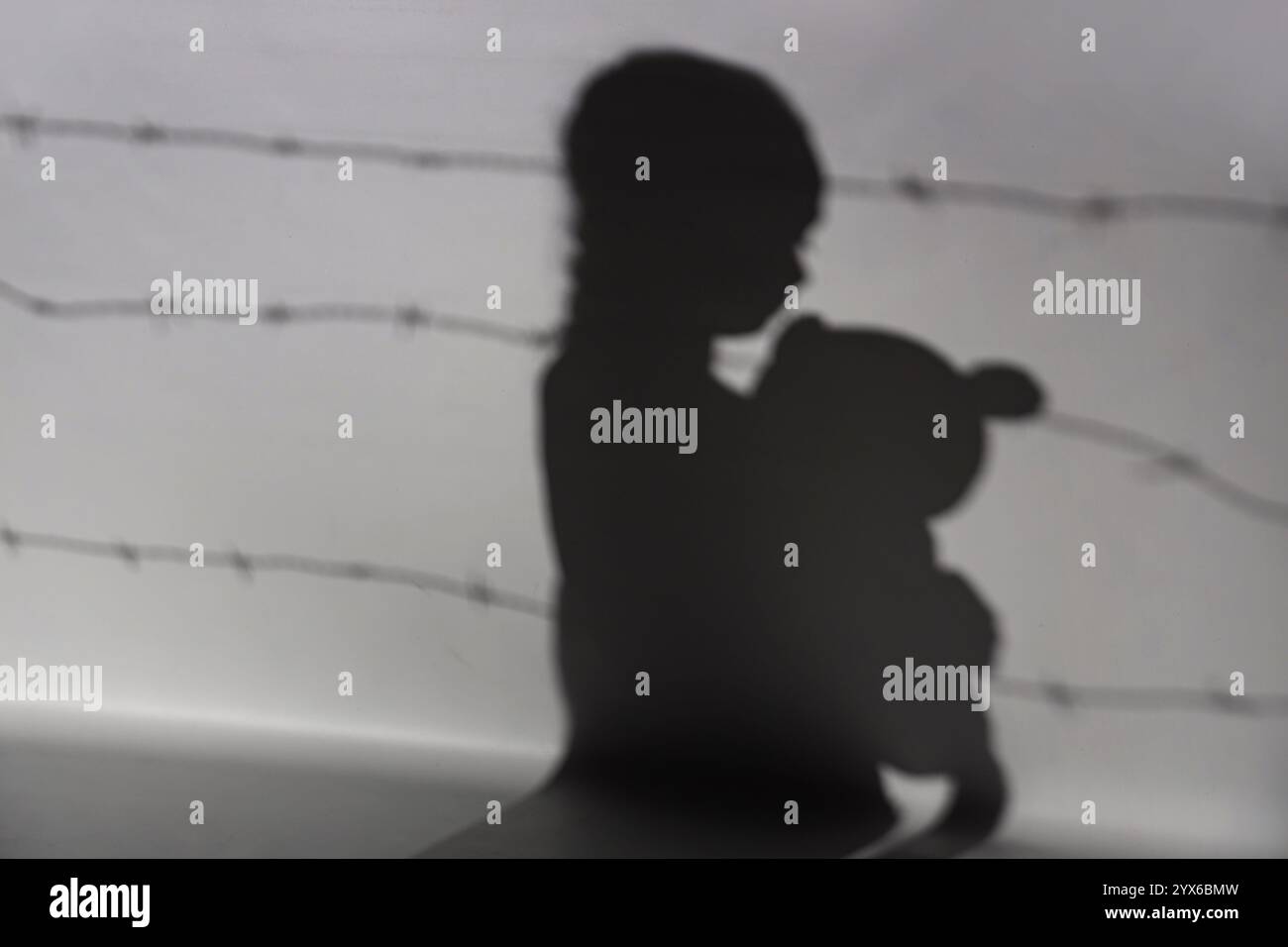 Shadow of little Jewish girl with toy and barbed wire on grey ...