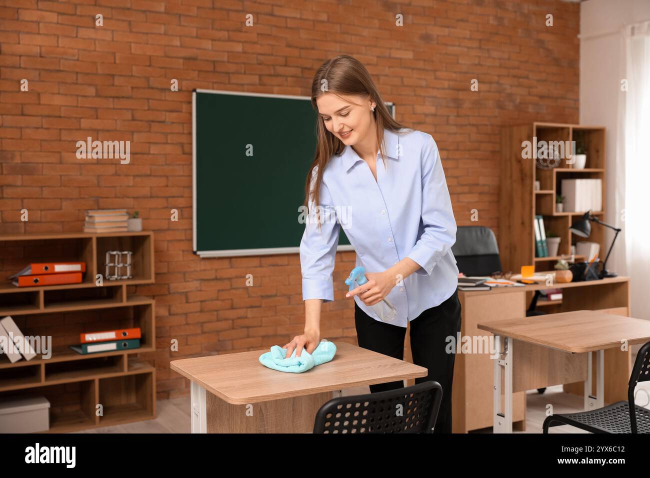 Female teacher wiping desk in classroom Stock Photo - Alamy