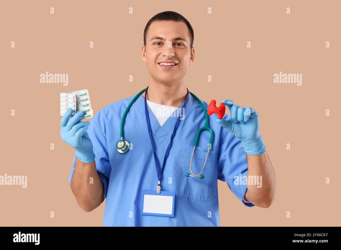Male endocrinologist with thyroid gland model and pills on beige ...