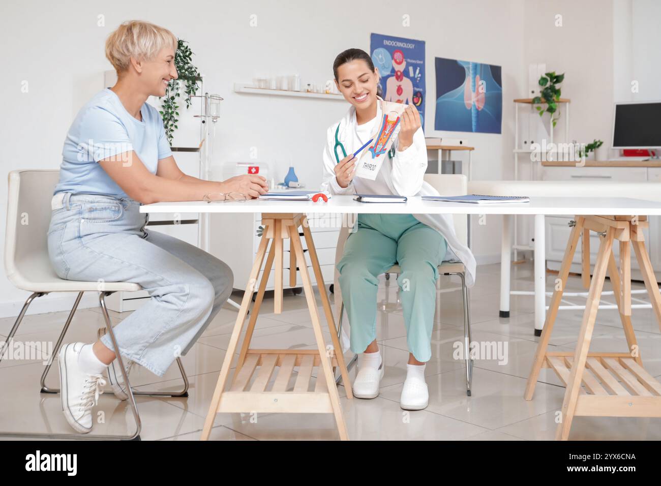 Female endocrinologist showing thyroid gland model to mature woman at ...
