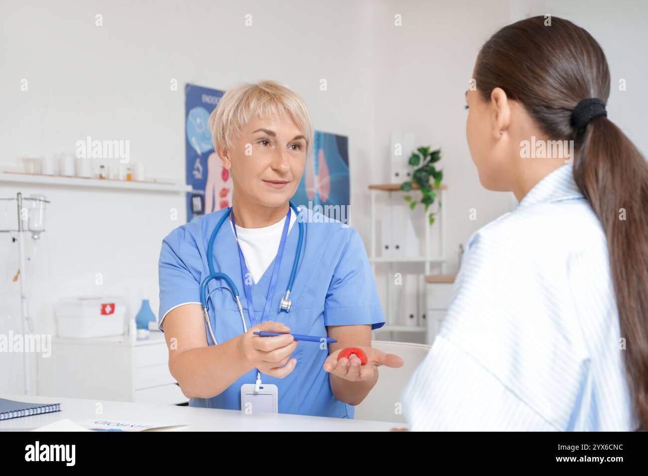 Female endocrinologist showing thyroid gland model to patient at table ...