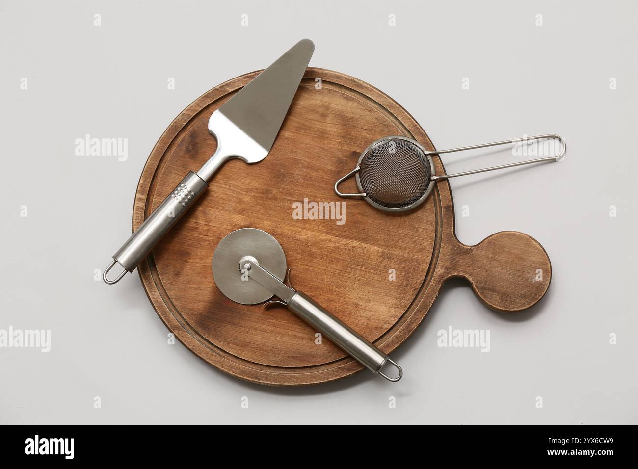 Wooden board with stainless steel pizza cutter, spatula and sieve on ...
