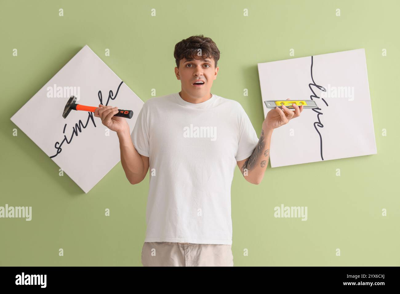 Confused young man with tools and overturned posters on green wall ...