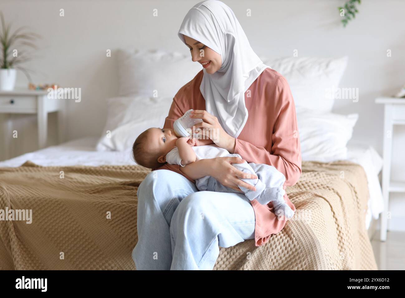 Happy Muslim mother in hijab feeding her cute little baby with milk ...