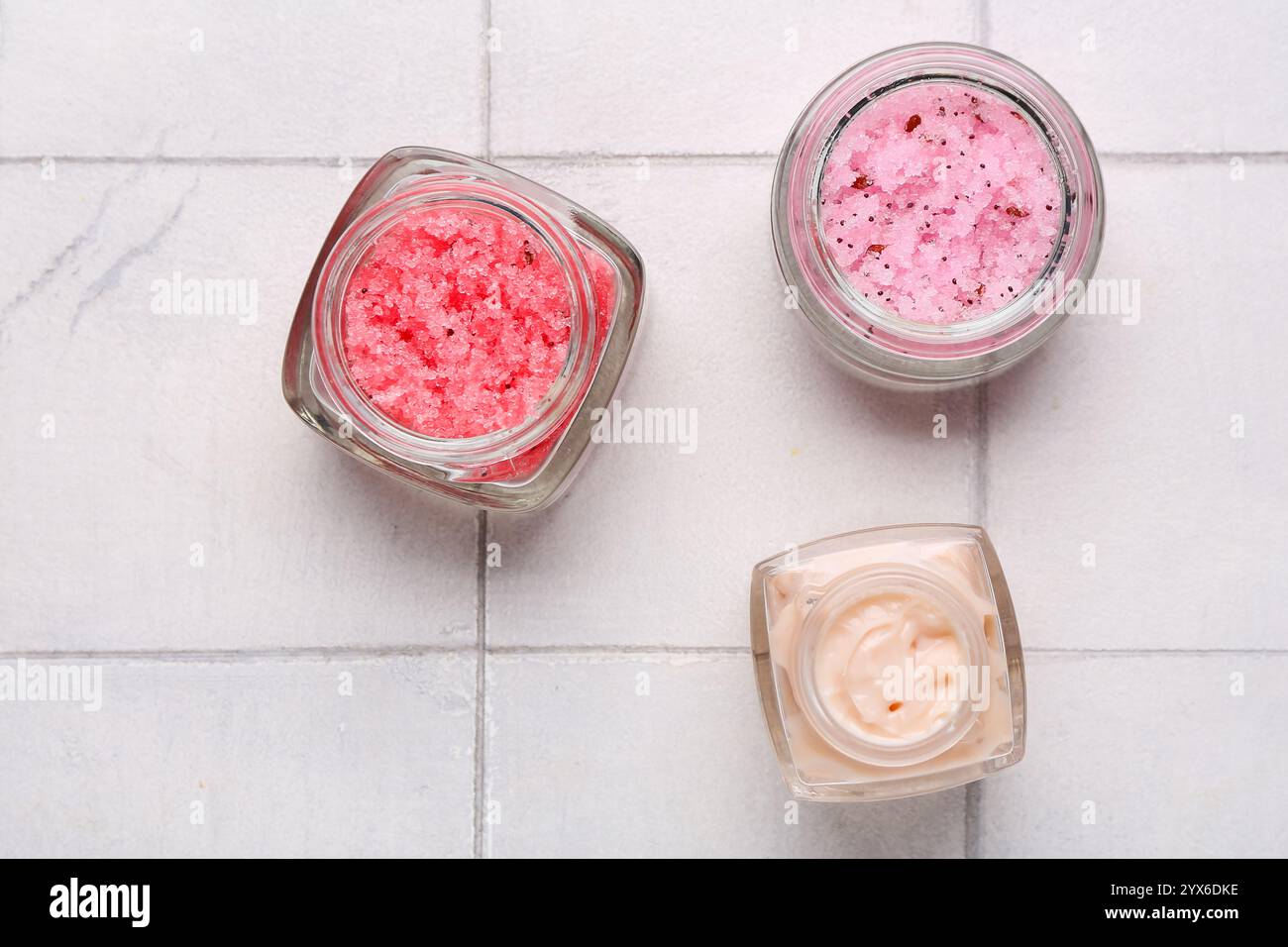Jars with scrubs and cosmetic cream on light tile background Stock ...
