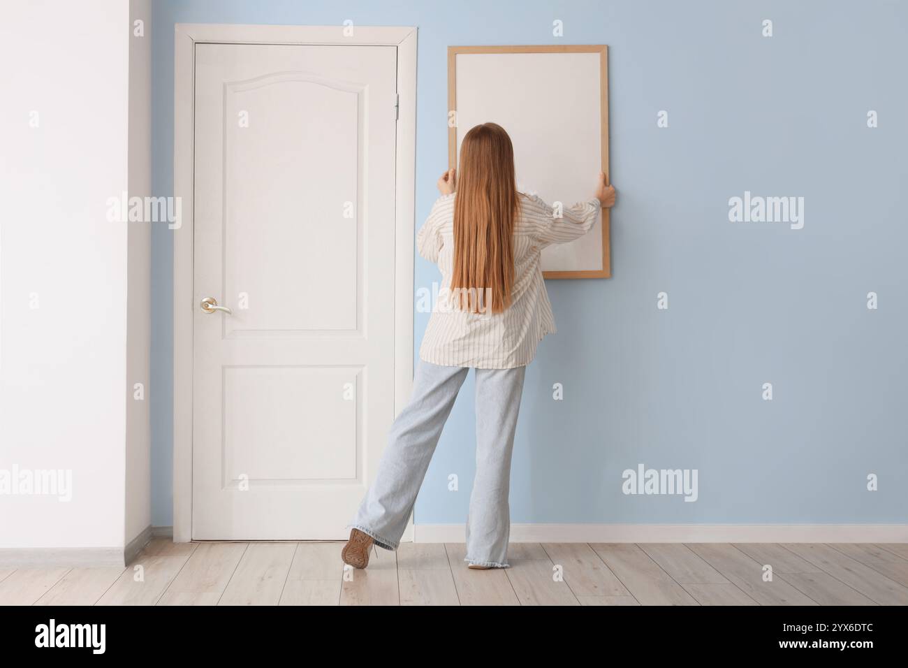Young woman hanging photo frame in hallway, back view Stock Photo - Alamy