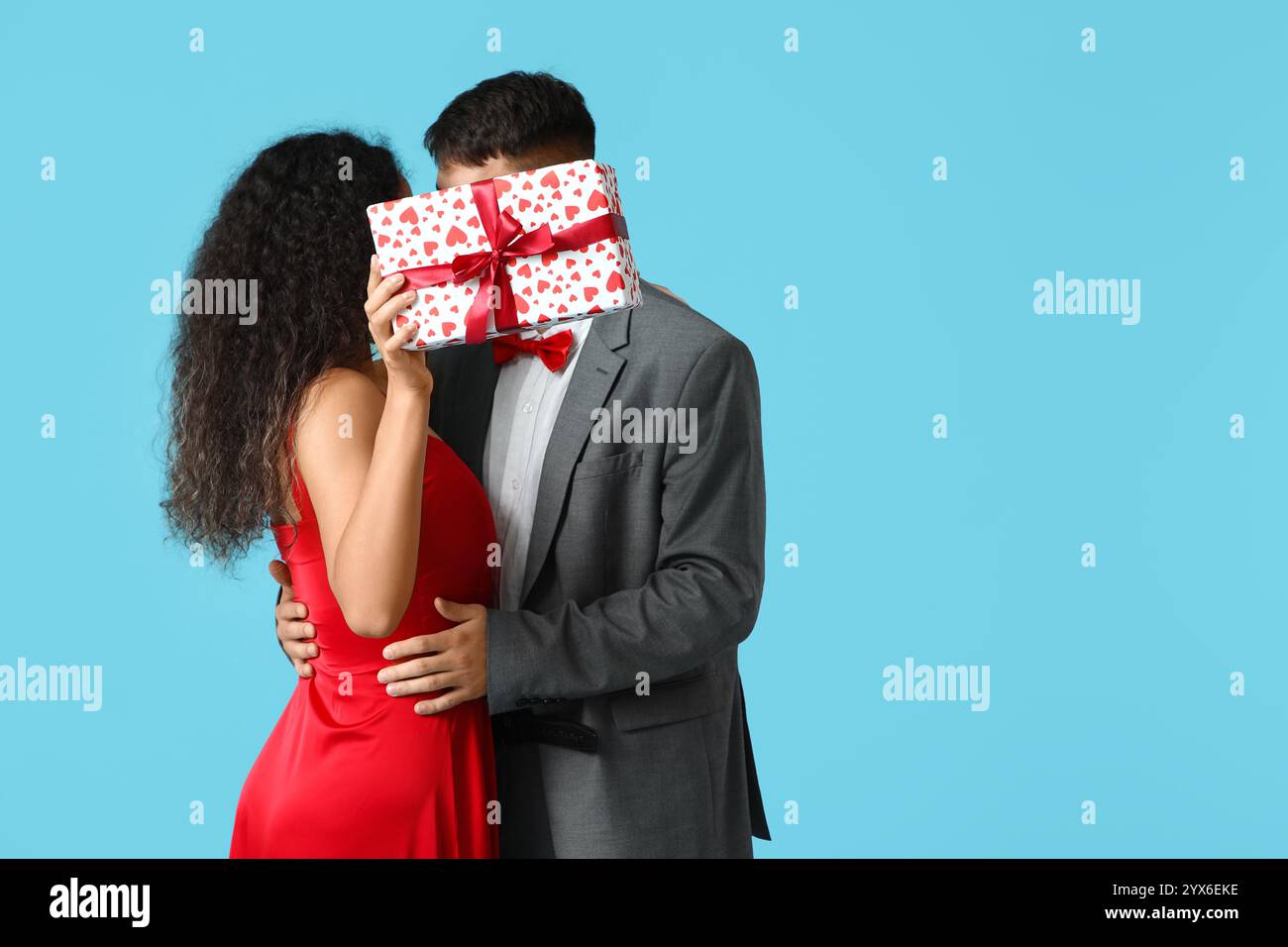 Loving young couple kissing behind gift boxes on blue background ...