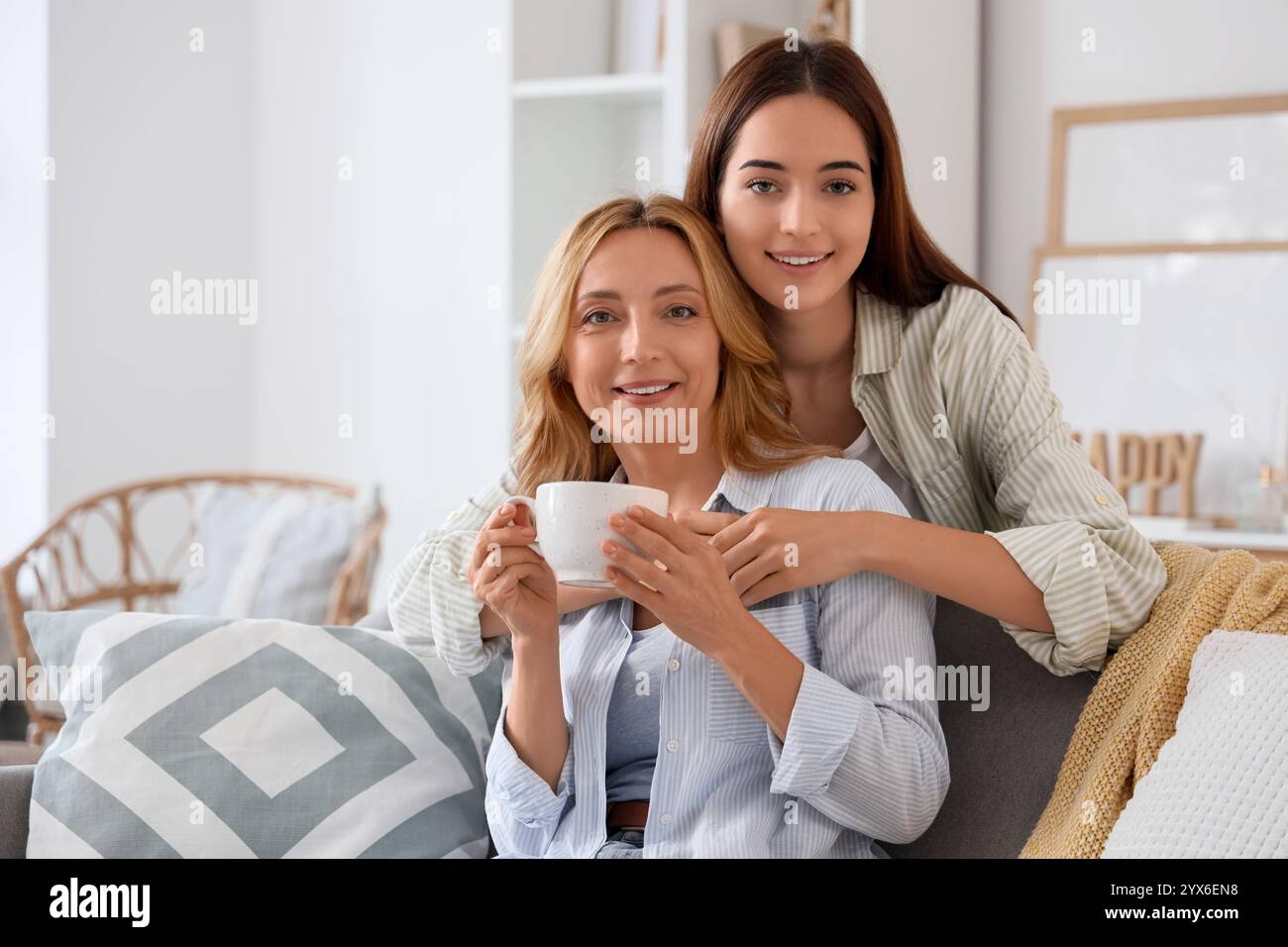 Young woman hugging her mother with cup of tea at home. International ...
